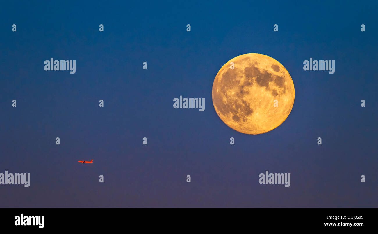 Plane flying across clear sky with full moon Stock Photo - Alamy