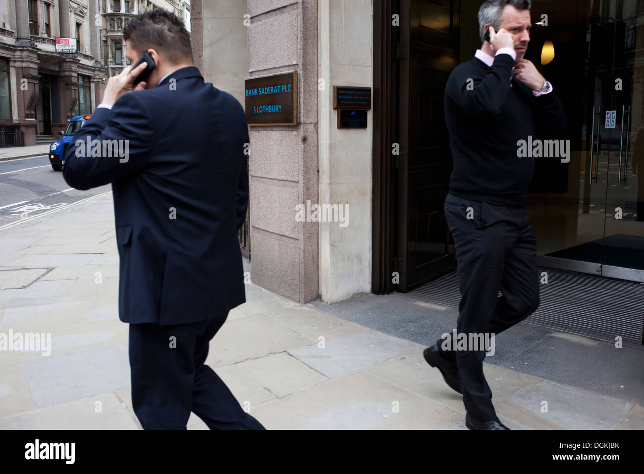 Two men on their mobile phones passing each other on a street corner ...