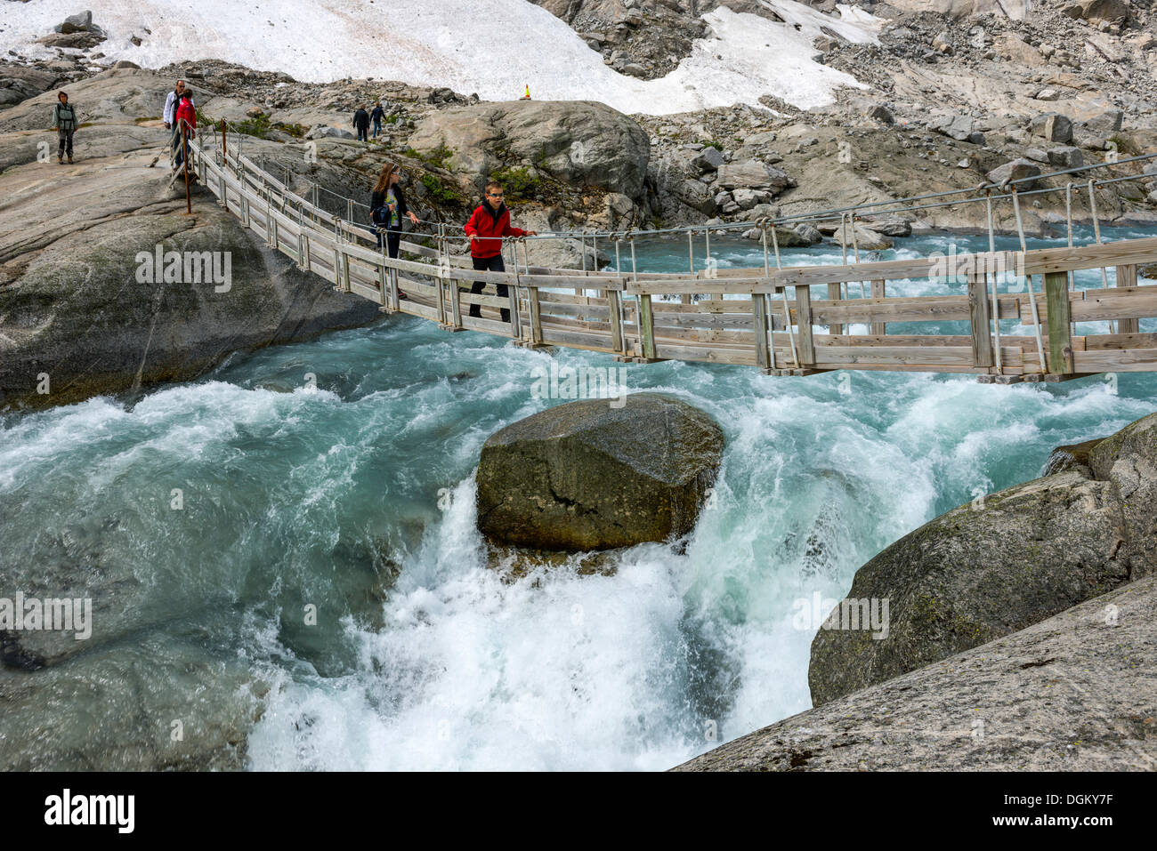 Hikers crossing a hanging bridge over a glacial river, glacier tongue ...