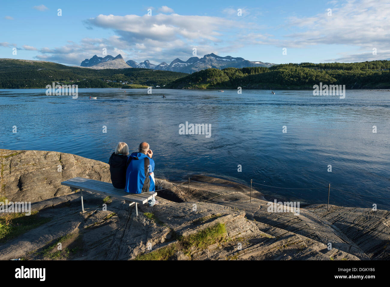 Couple sitting on a bench looking out to the tidal Saltstraumen strait ...