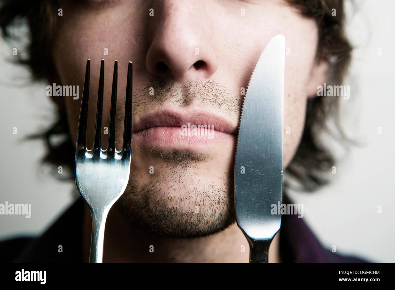 Young man holding a knife and a fork in front of his face, Germany ...