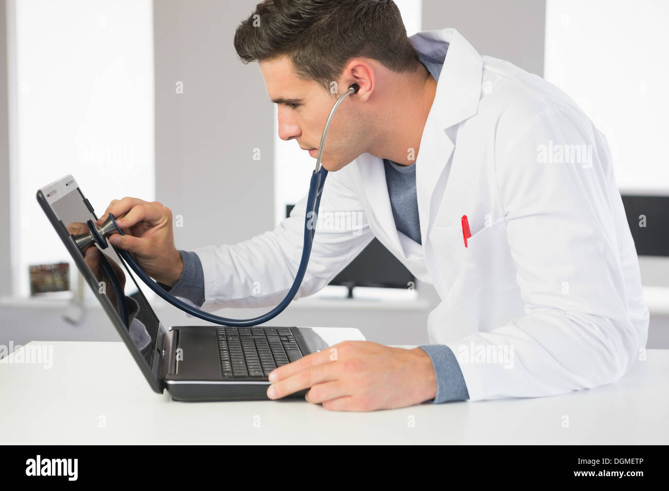 Attractive focused computer engineer examining laptop with stethoscope ...