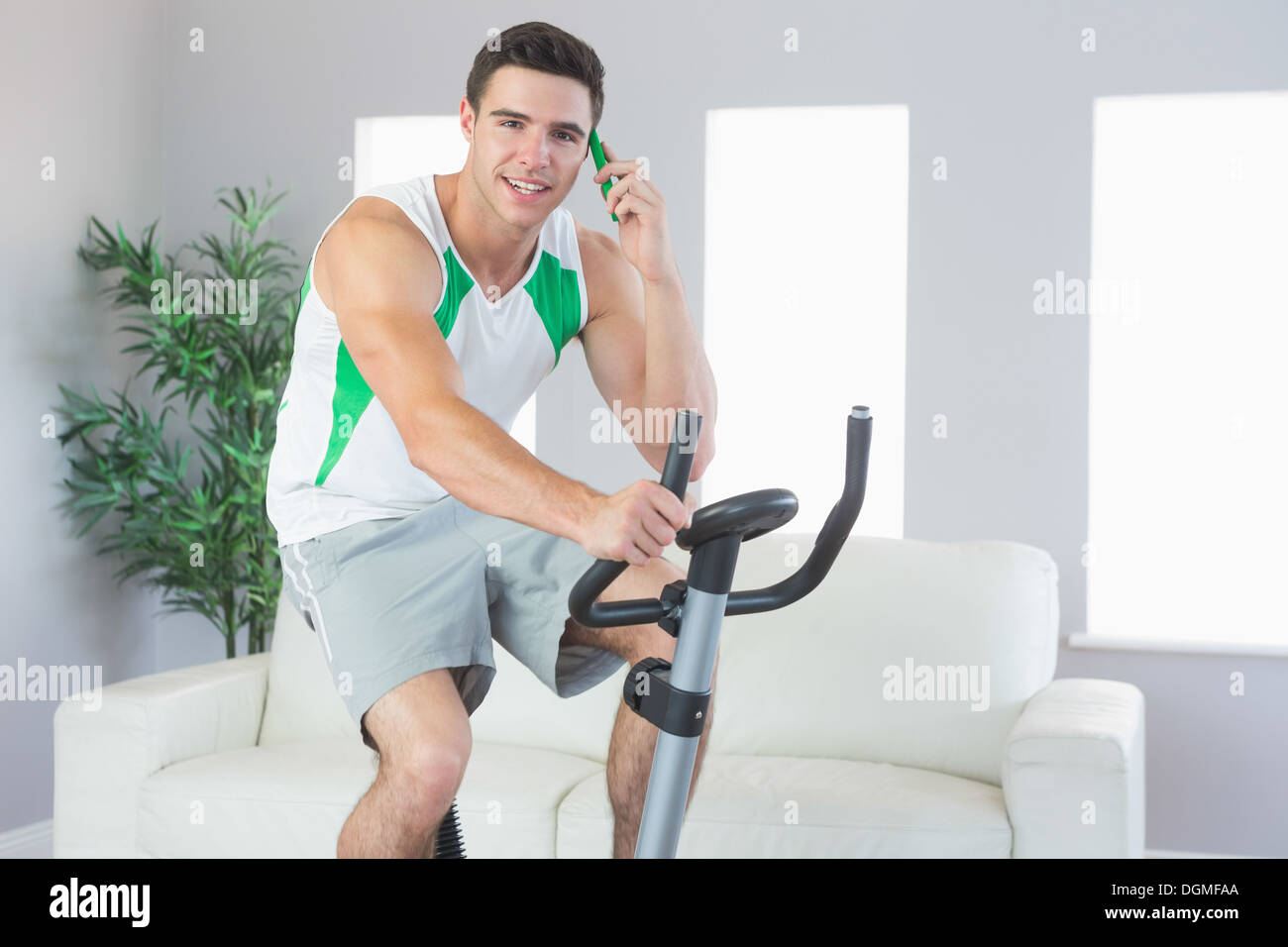 Smiling handsome man training on exercise bike phoning Stock Photo - Alamy