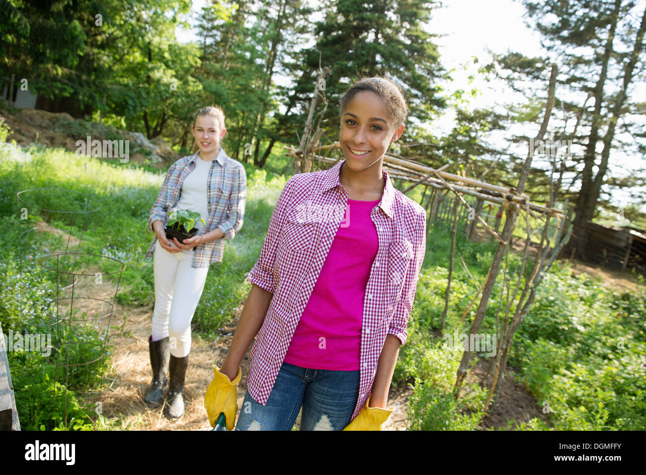 Two girls in a garden, walking up the path, one carrying a plant in a ...