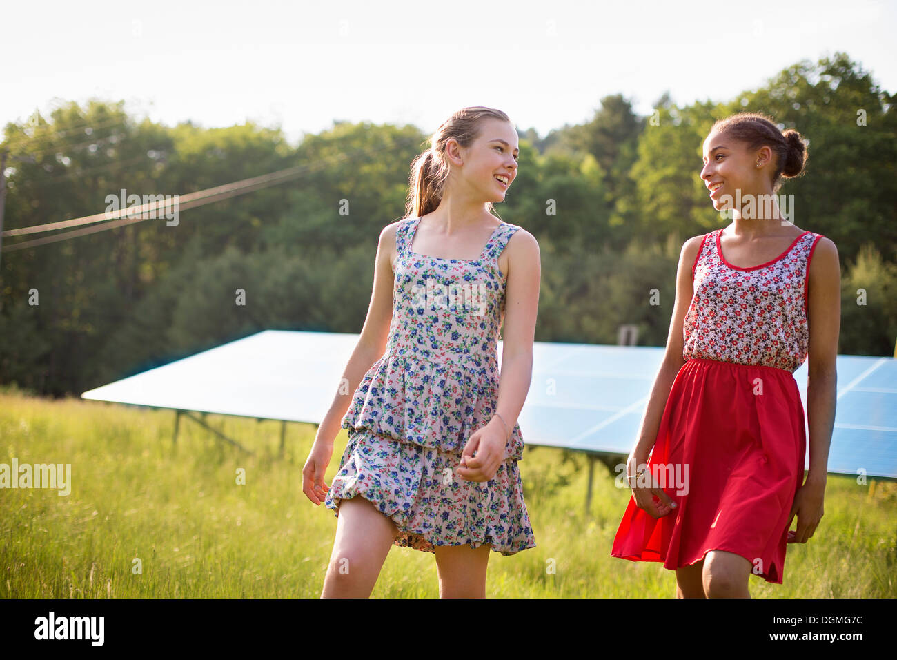 Two young girls on the farm, outdoors. A large solar panel in the field ...