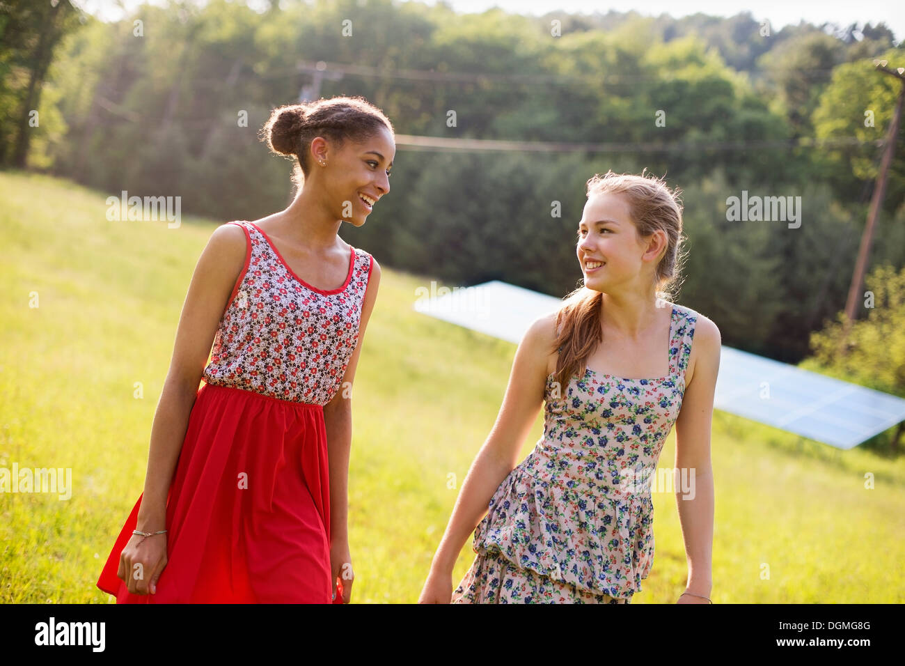 Two young girls on the farm, outdoors. A large solar panel in the field ...