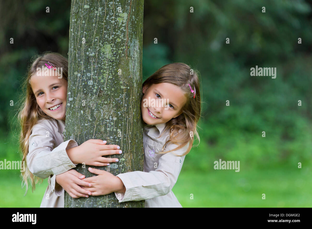 Twin girls, 9, looking from the left and the right behind a tree Stock ...