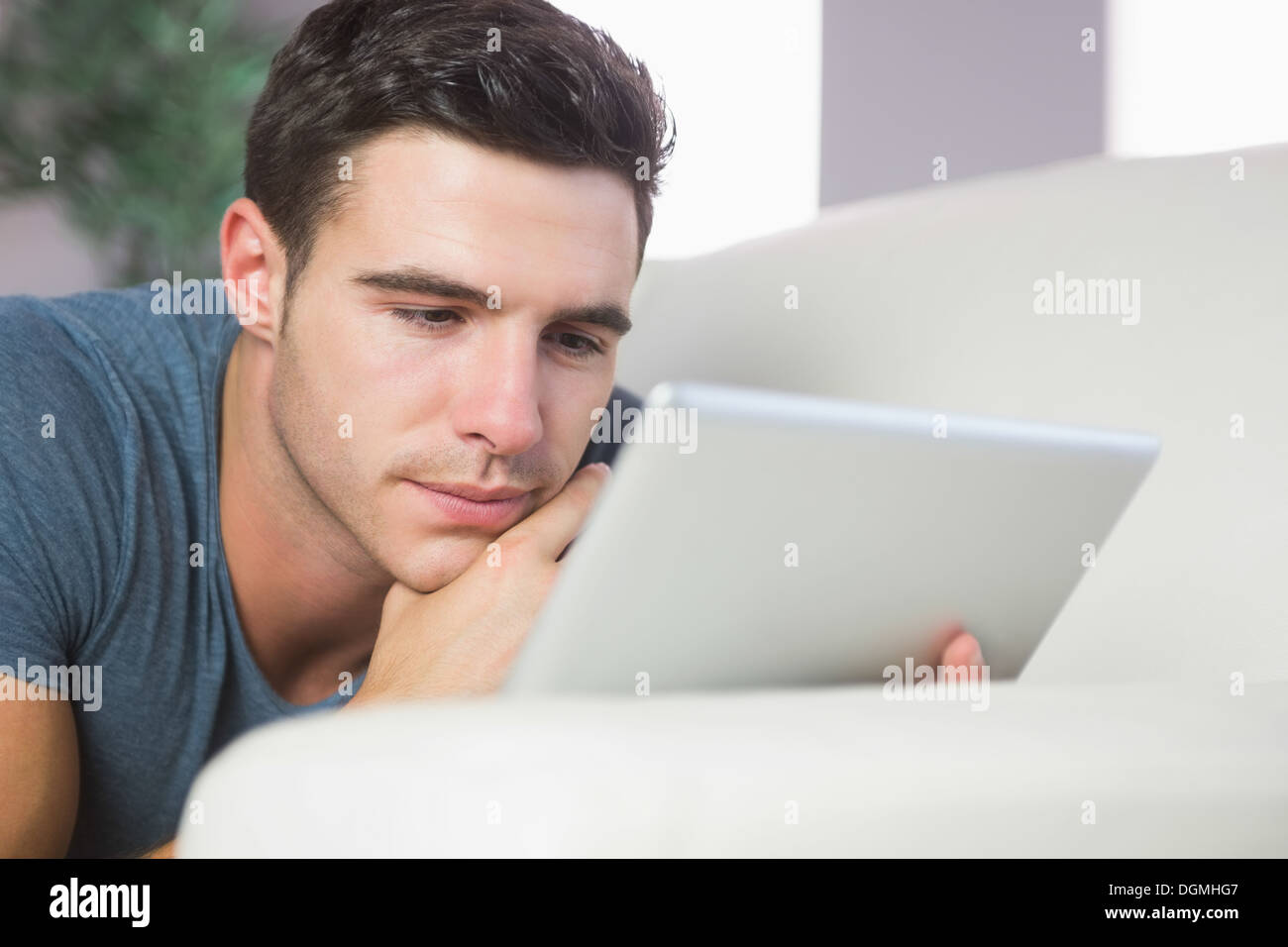 Focused handsome man lying on couch using tablet Stock Photo - Alamy