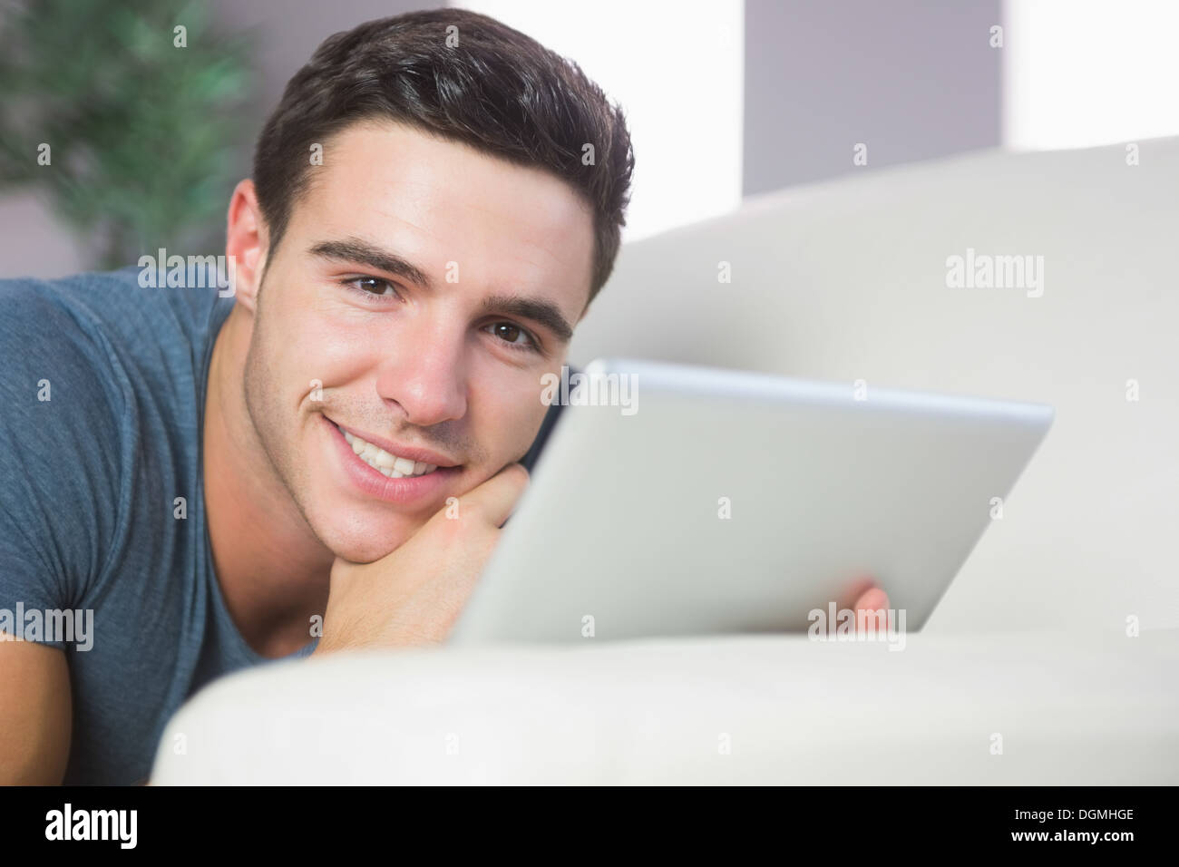 Cheerful handsome man lying on couch using tablet Stock Photo - Alamy