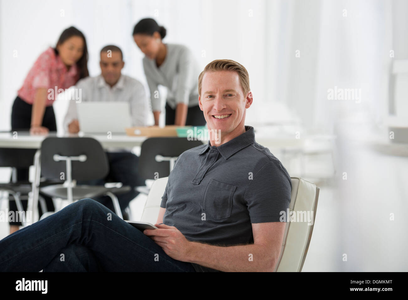 Business. Four people, one man sitting on a soft chair, and three ...