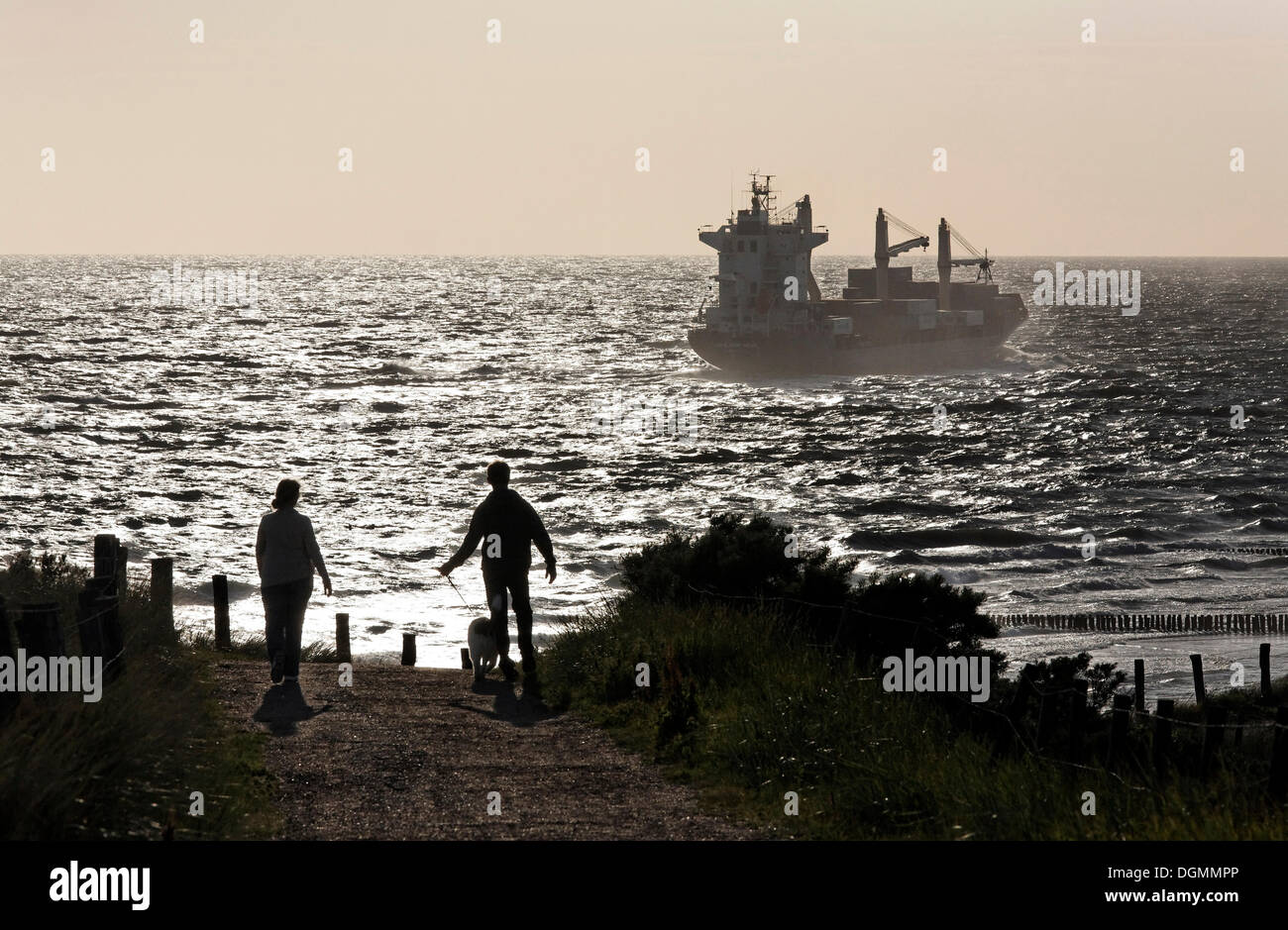 A couple taking a walk on the dunes, a cargo boat on the ocean ...