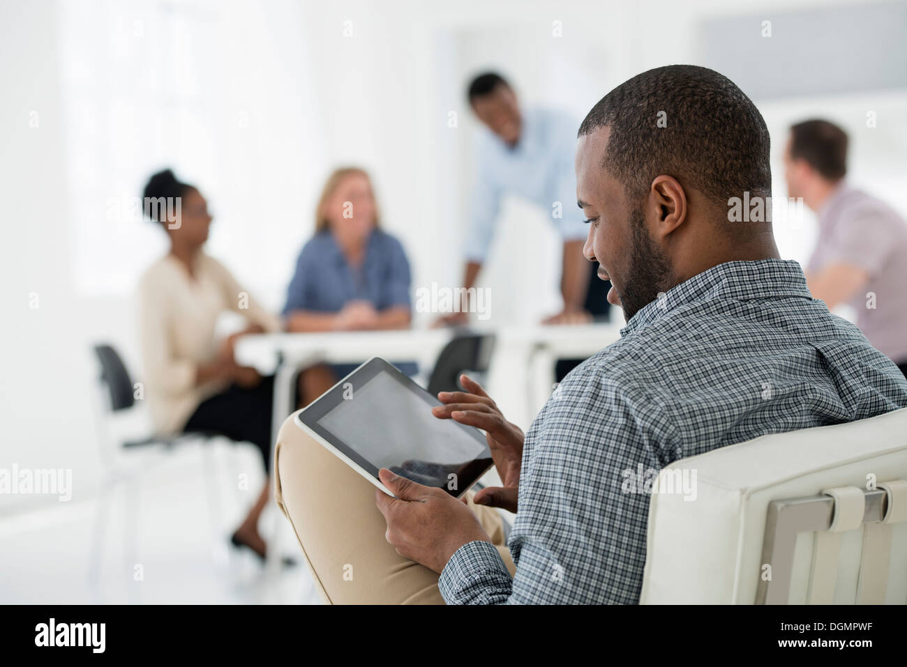 Office interior. Meeting. One person seated separately, using a tablet ...