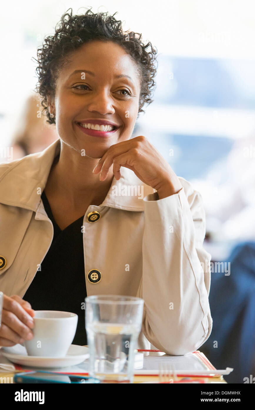 City life. A woman wearing a beige jacket sitting at a table in a cafe ...