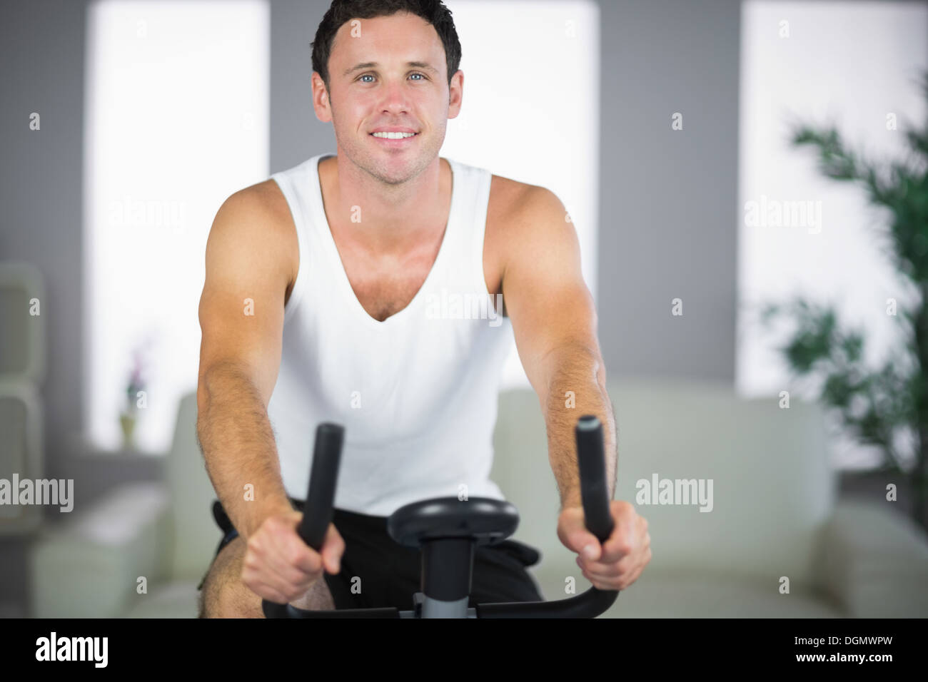 Attractive fit man exercising on bike smiling at camera Stock Photo - Alamy
