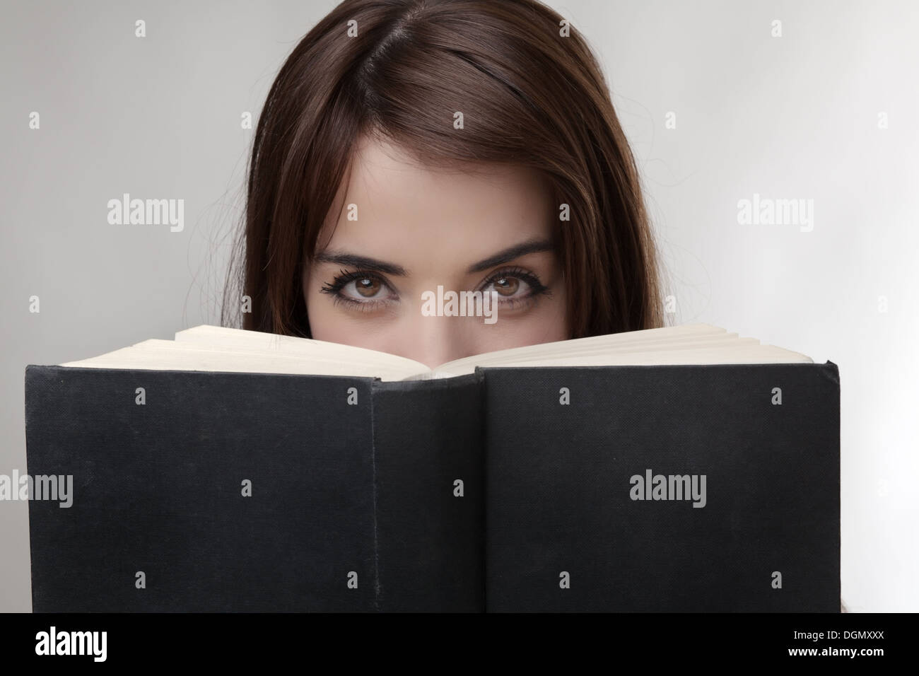 just woman eyes peering over a hard back book Stock Photo - Alamy