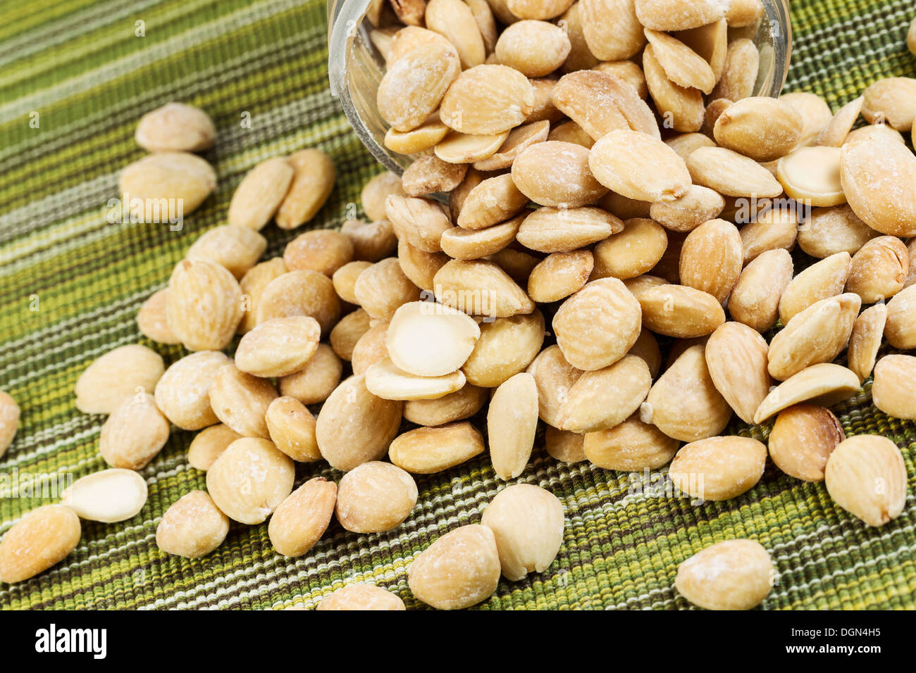 Horizontal photo of unshelled salted almonds spilled out of jar onto ...