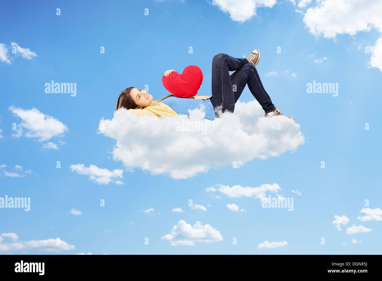 Young thoughtful female holding a heart and lying on clouds Stock Photo ...