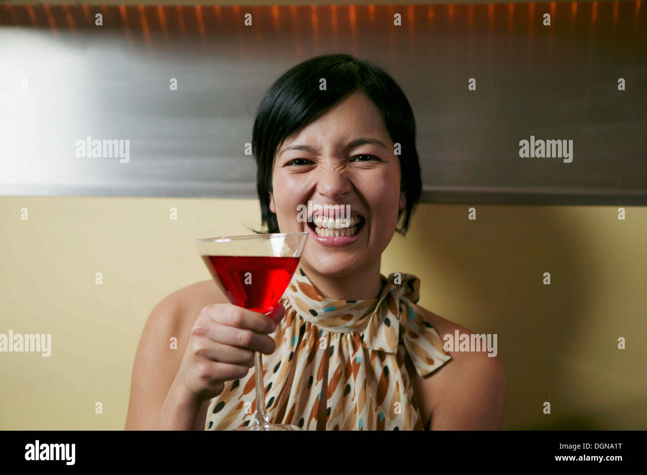 A young woman sitting in a bar holding a cocktail glass, making a funny ...