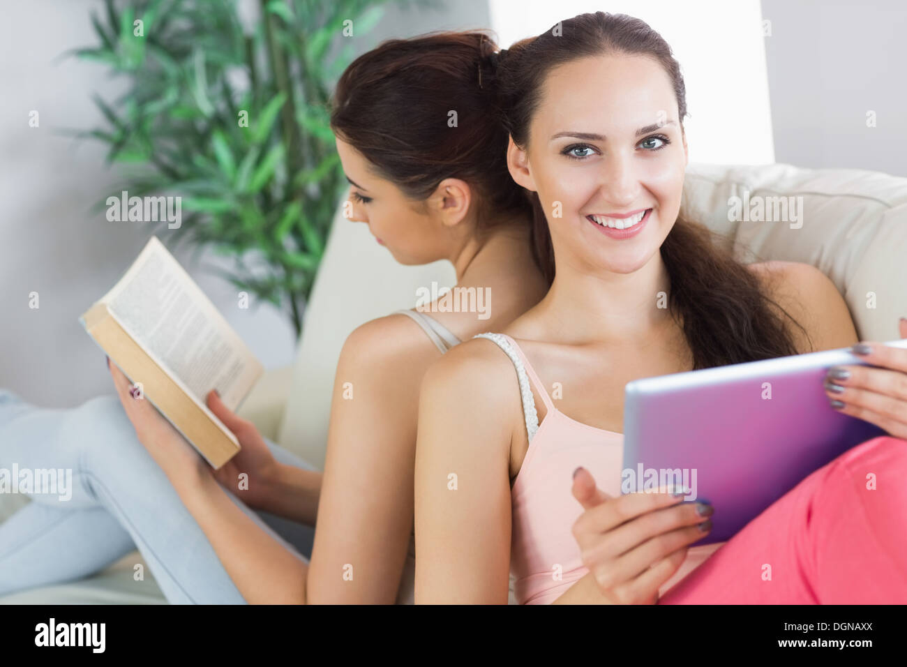 Two pretty friends sitting on back to back on the couch Stock Photo - Alamy