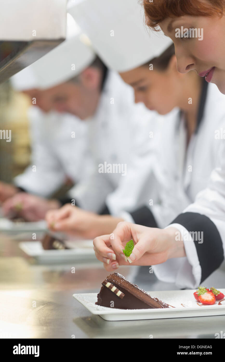 Team of young chefs in a row garnishing dessert plates Stock Photo - Alamy