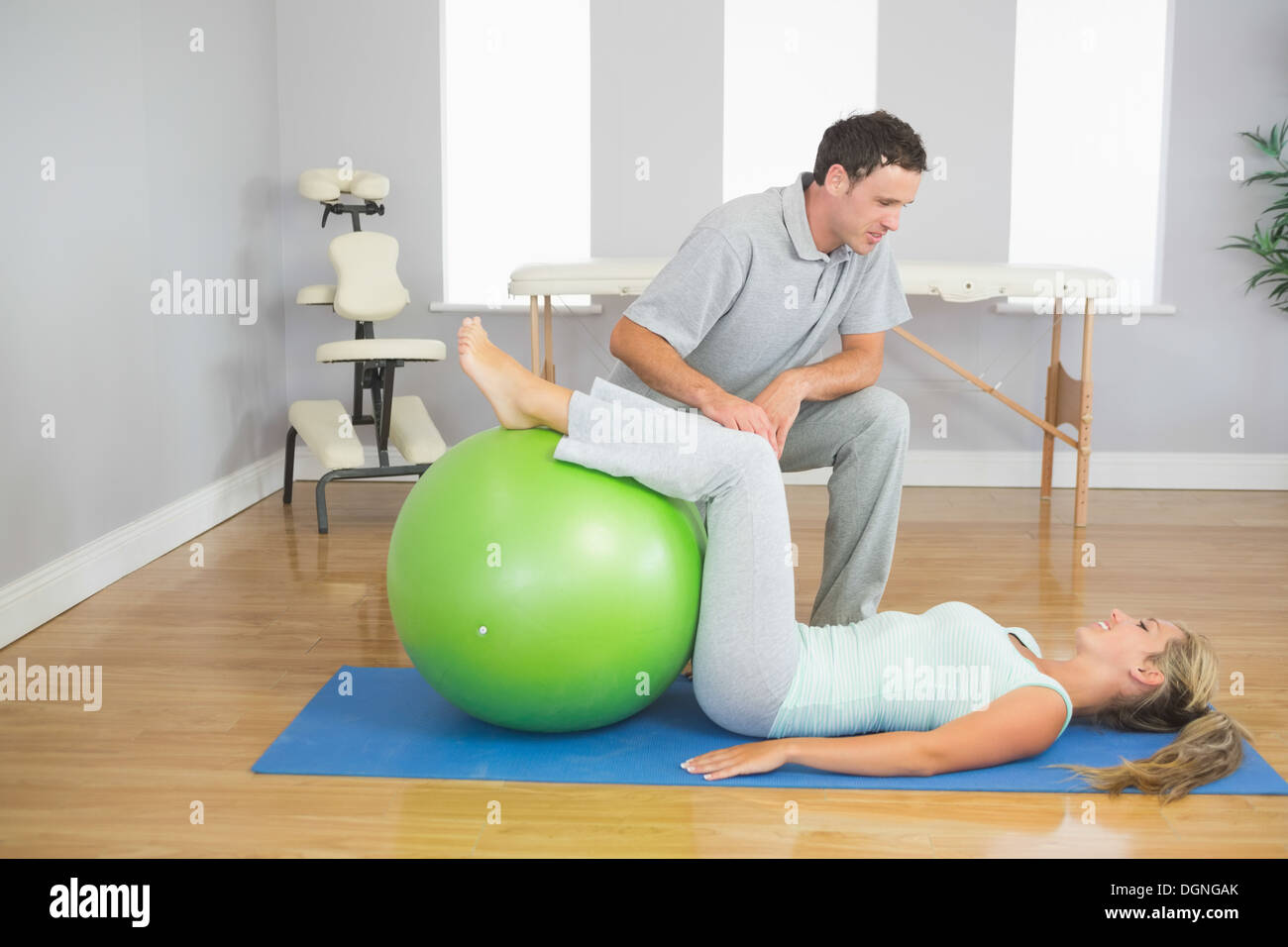 Physiotherapist checking patient doing exercise with exercise ball ...