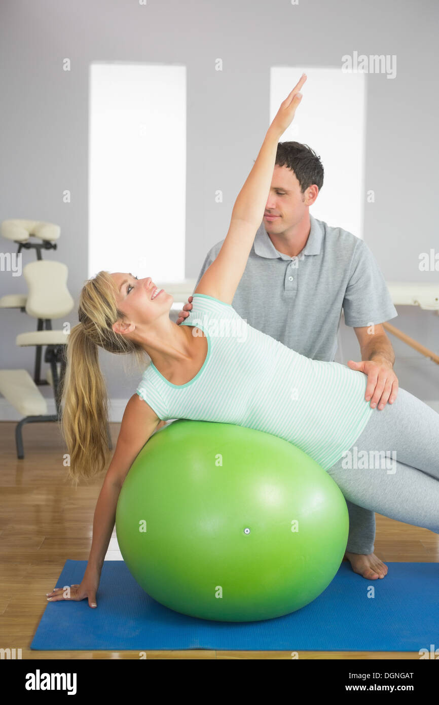 Smiling physiotherapist correcting patient doing exercise on exercise ...