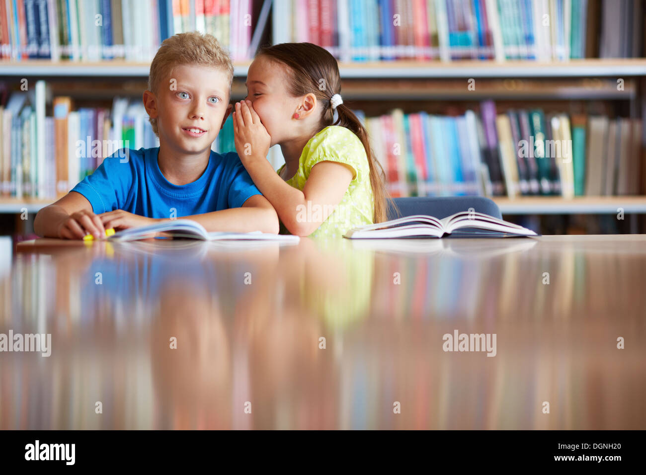 Portrait of cute schoolgirl whispering something to her classmate in ...