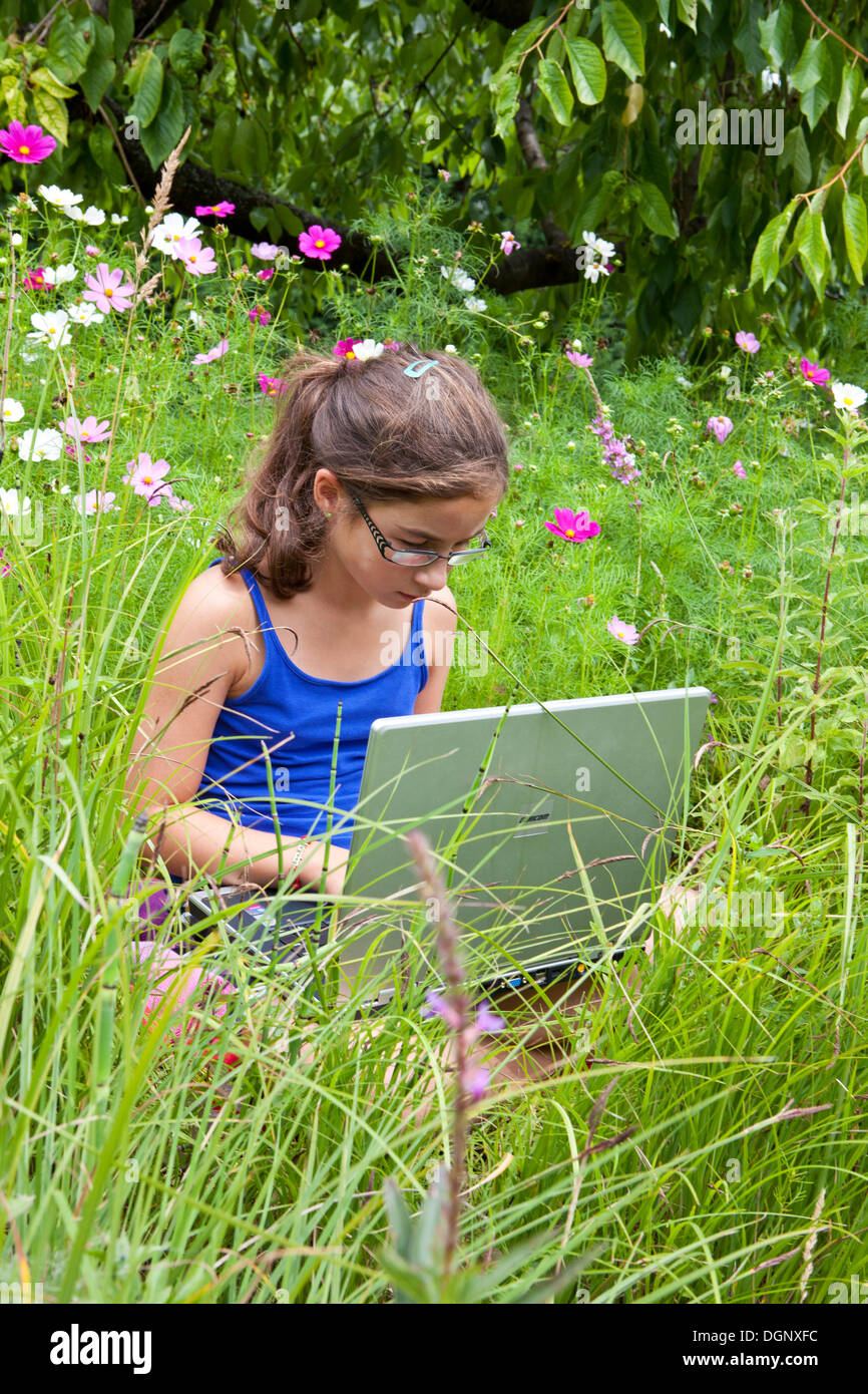 Girl, 11 years, working on a laptop computer, notebook, sitting in a ...