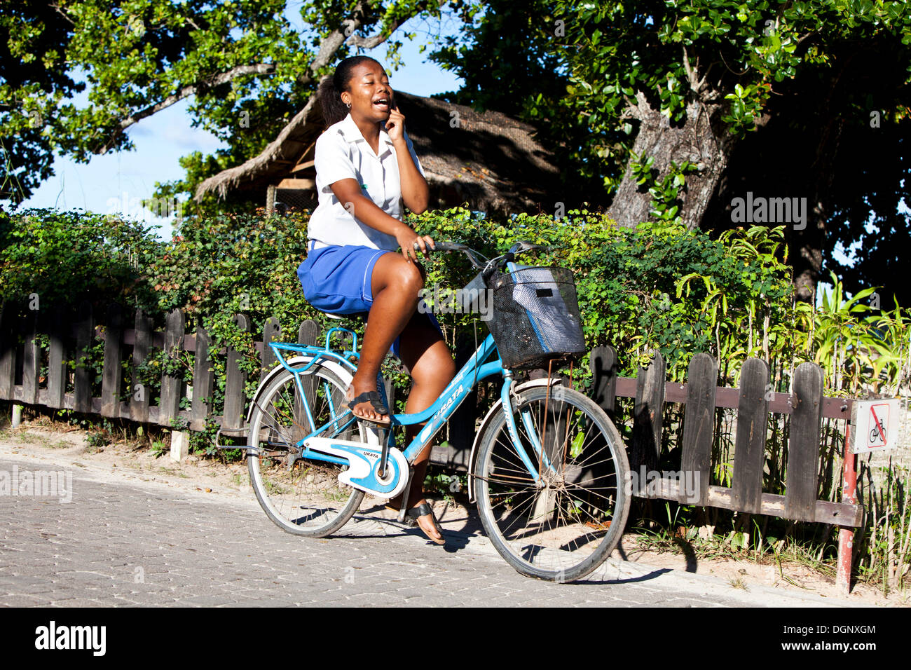 Woman talking on a mobile phone while riding a bicycle, La Digue Island ...