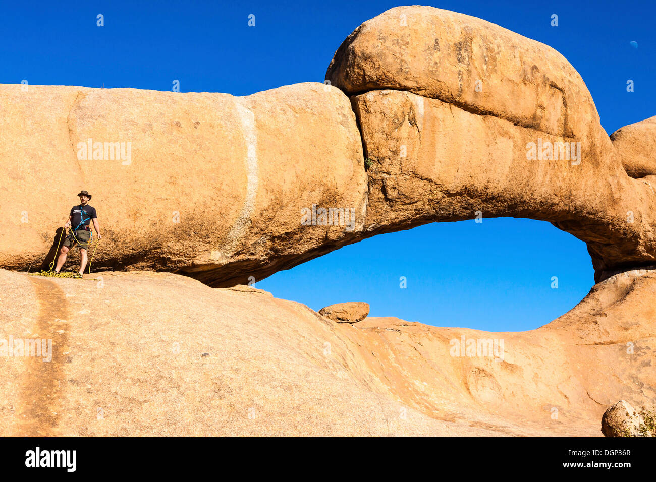 Young man climbing a rock arch, near the Spitzkoppe granite peaks ...
