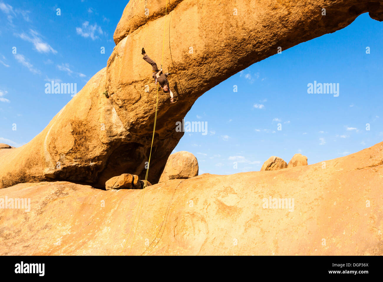 Young man abseiling from a rock arch, hanging upside down, near the ...