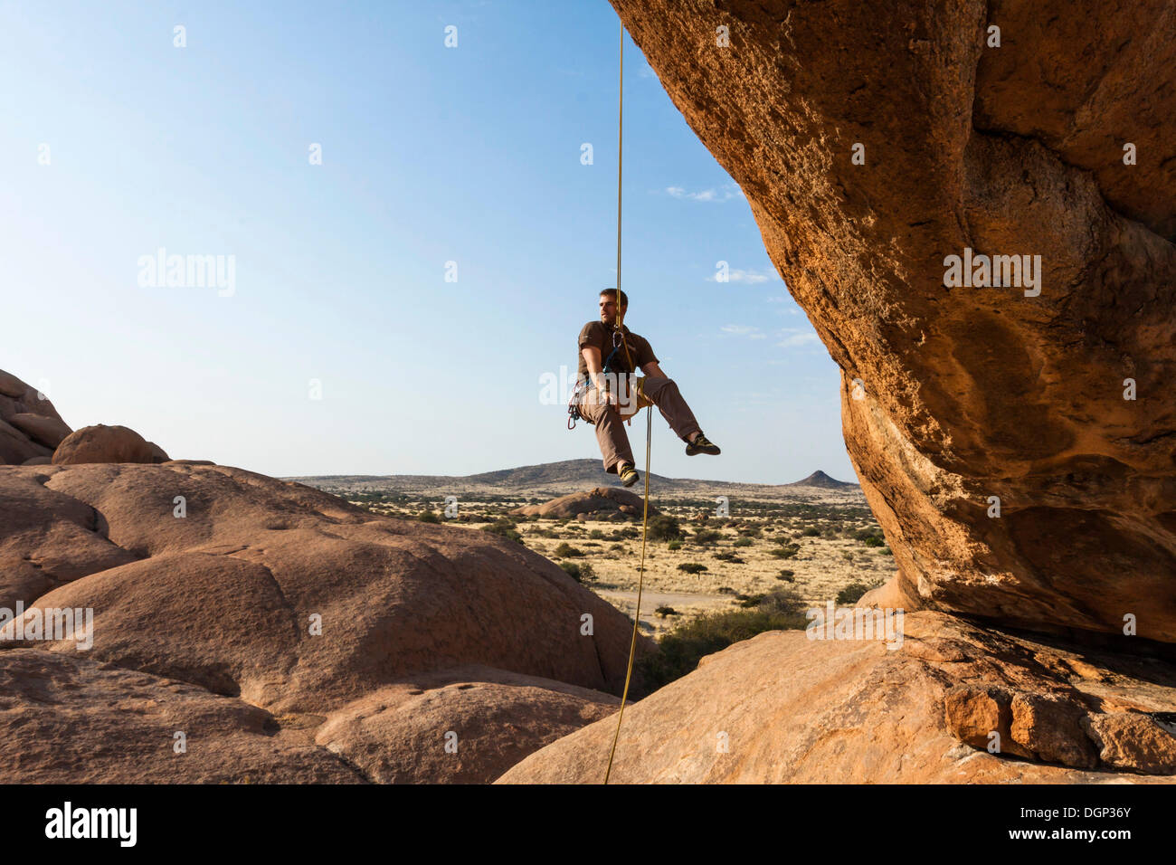 Young man abseiling from a rock arch, near the Spitzkoppe granite peaks ...