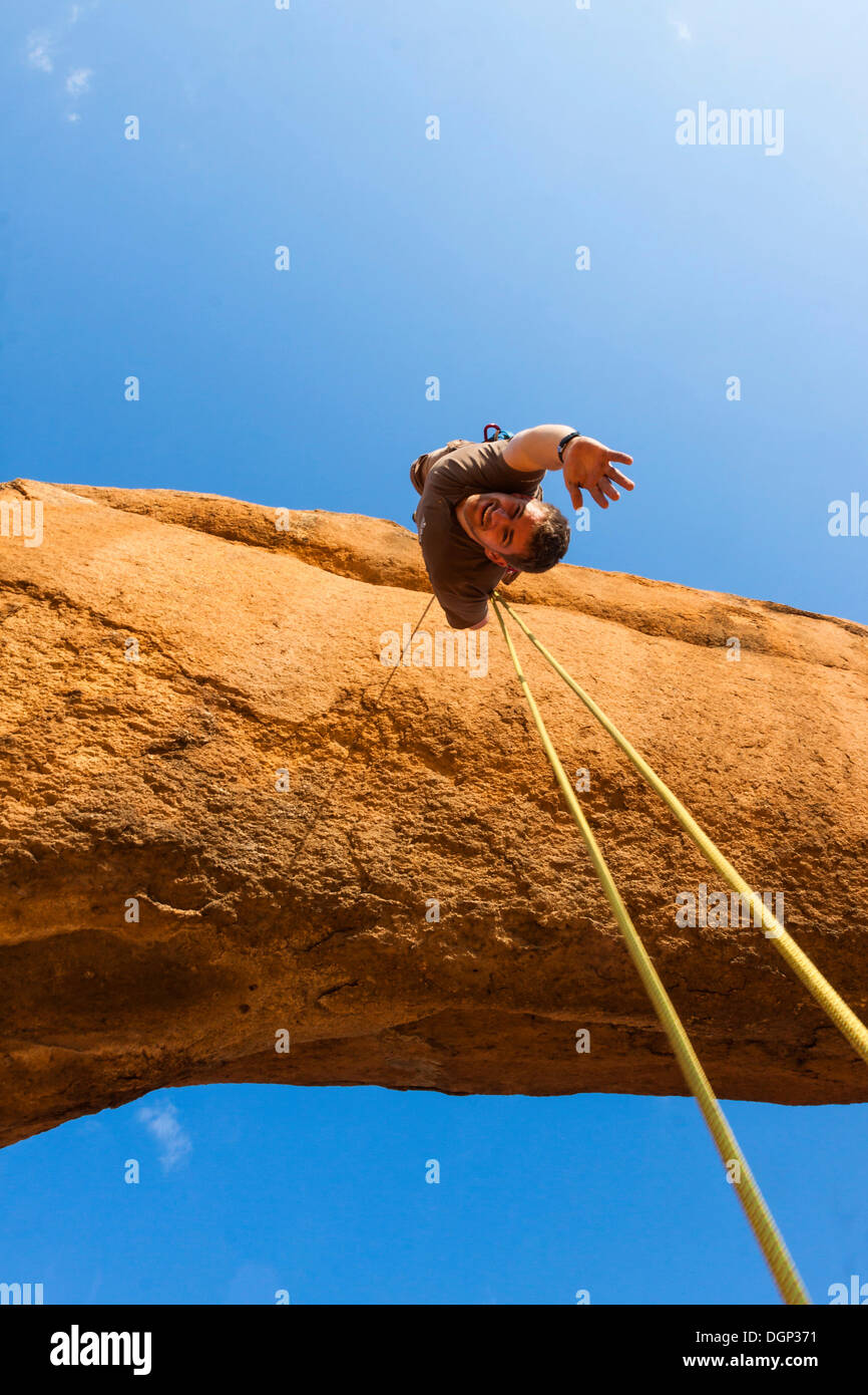 Young man abseiling from a rock arch, hanging upside down, near the ...