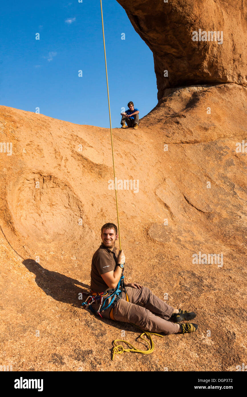 Young man abseiling from a rock arch, hanging upside down, near the ...