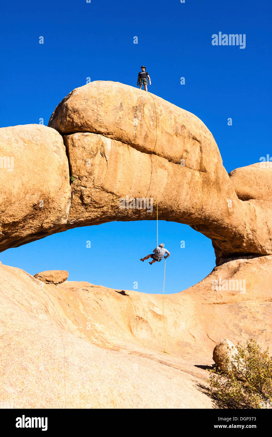 Two men abseiling from a rock arch, near the Spitzkoppe granite peaks ...