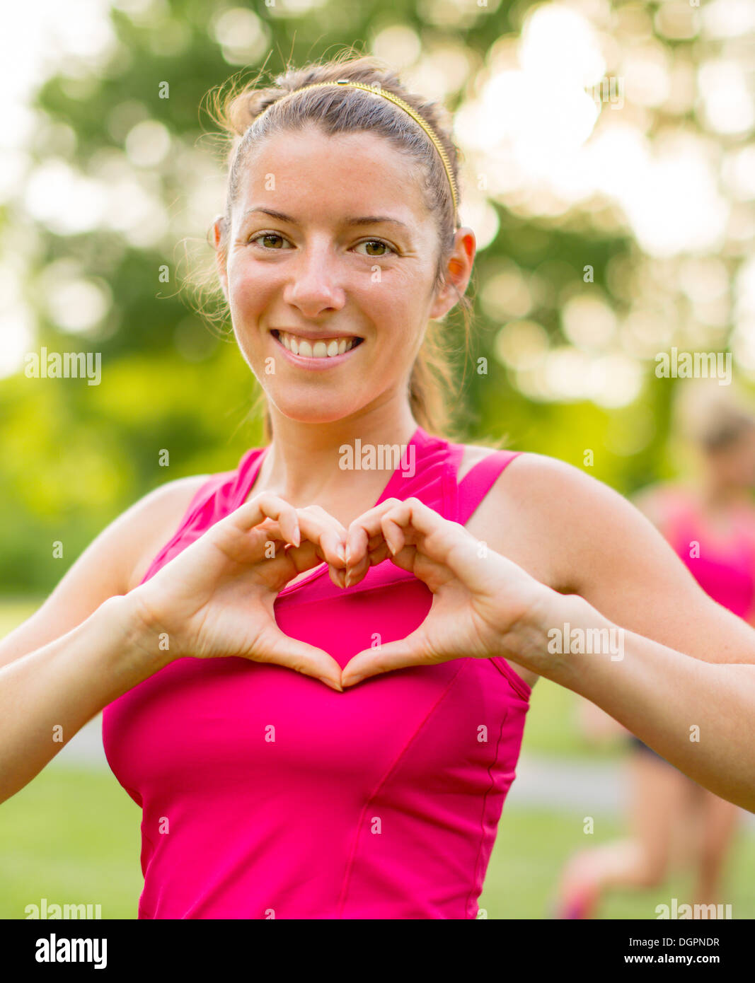 Smiling portrait of a young woman making a heart sign with her hands ...