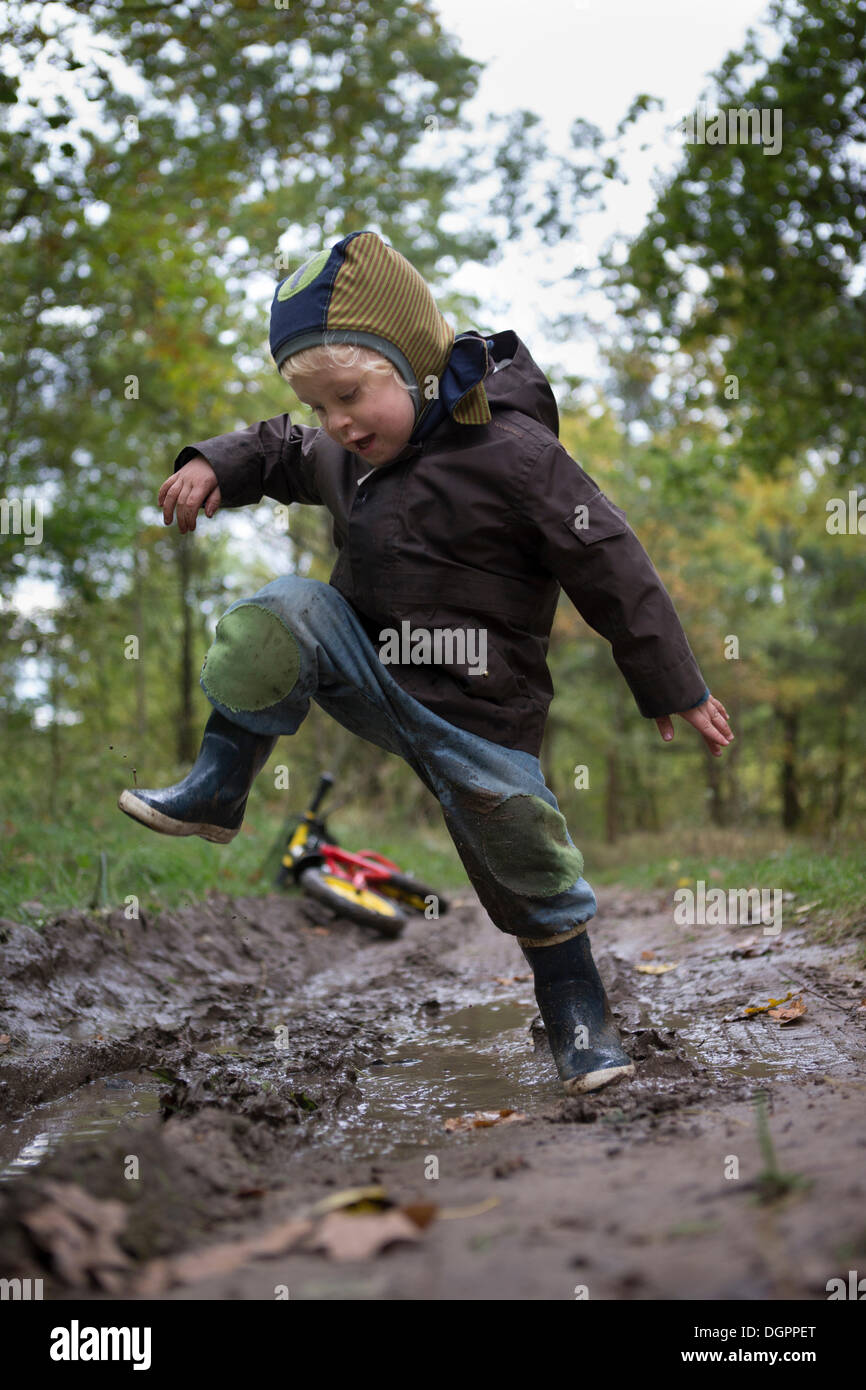 Little boy jumping with joy into a muddy puddle during an autumn walk ...