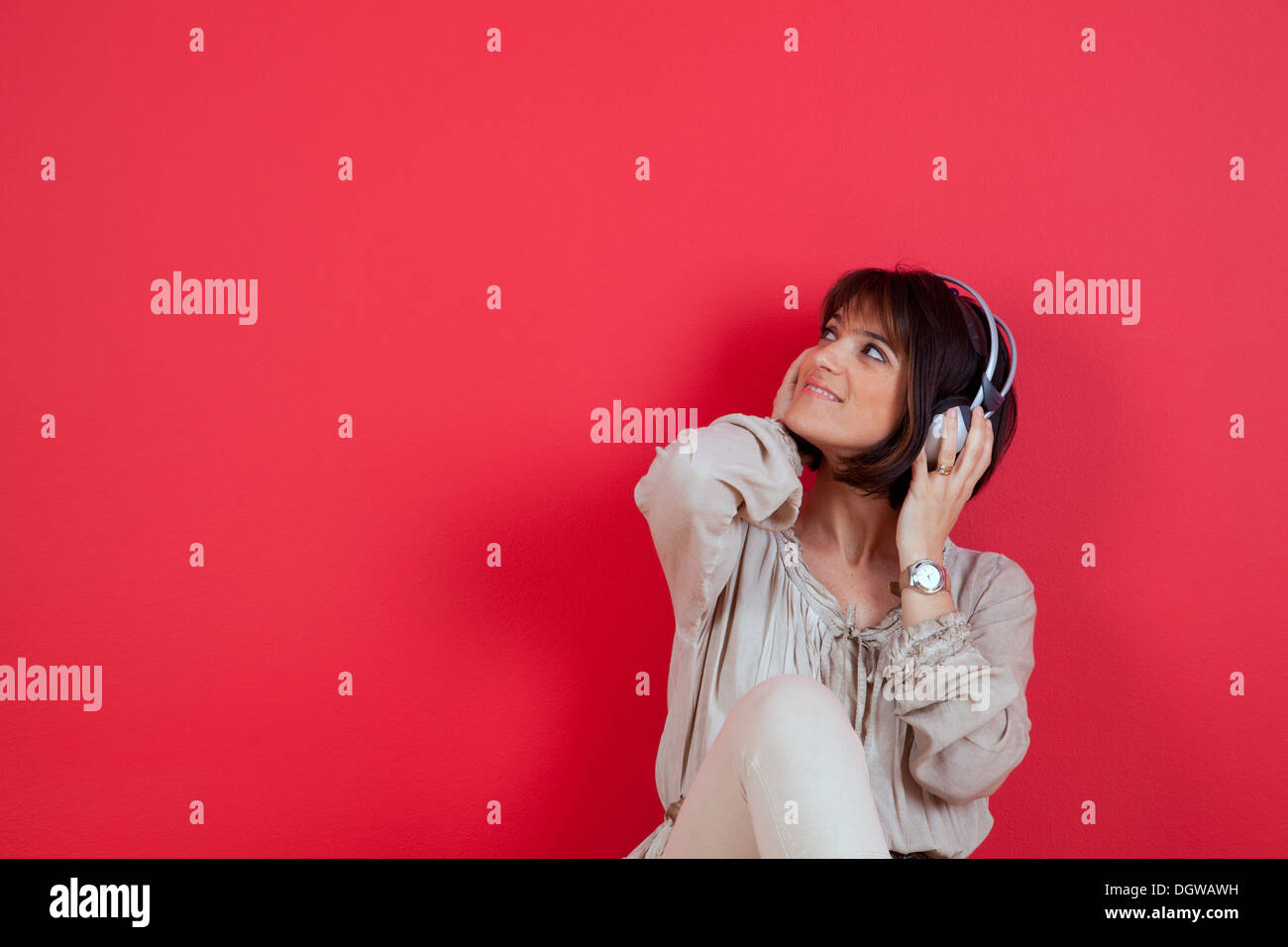 Woman listening to music with headphones next to a red wall Stock Photo ...