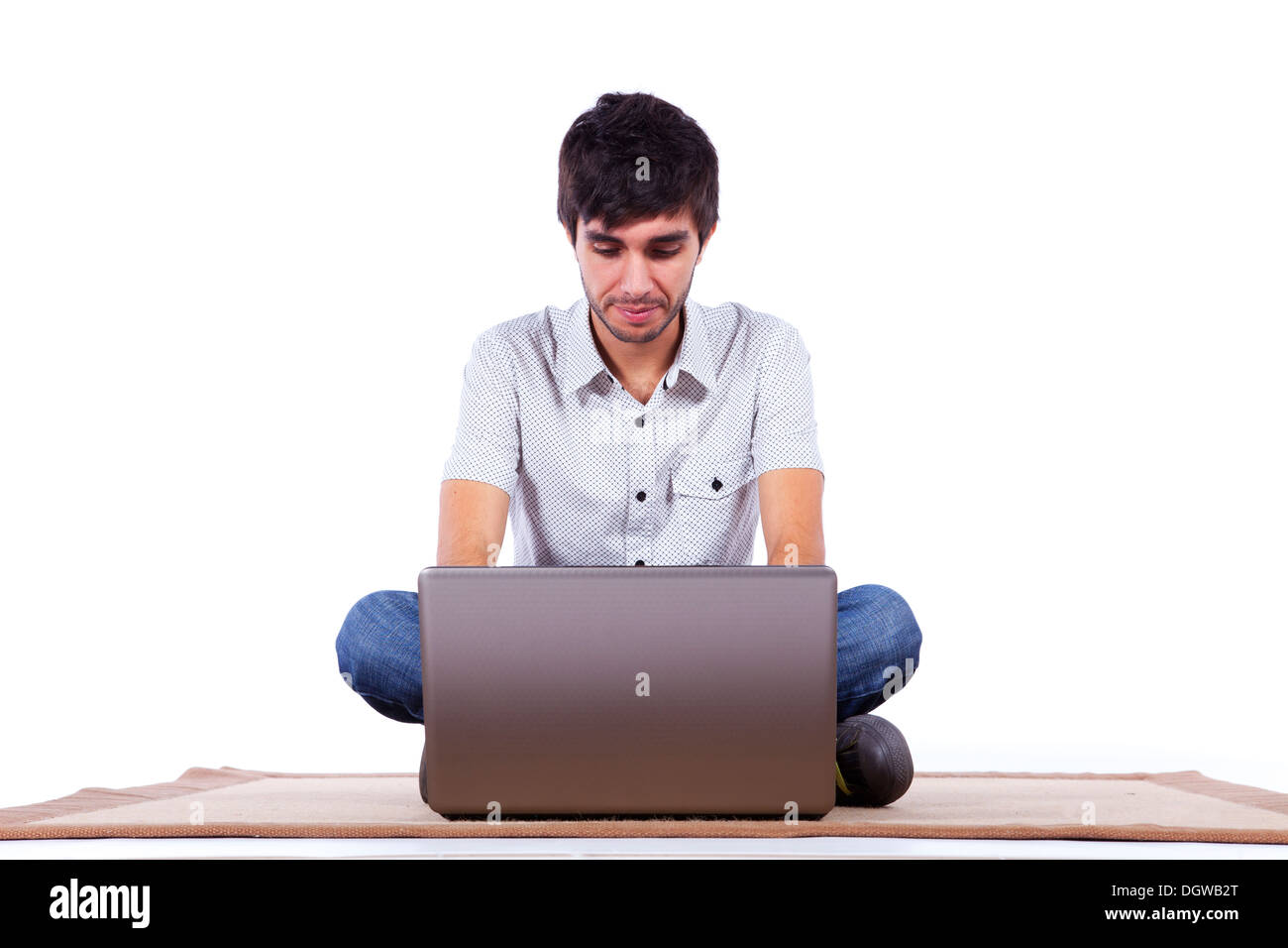 young man surfing the internet in his laptop sited on the carpet ...