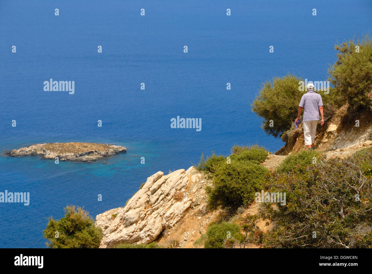 Woman hiking along a steep coastal cliff trail, looking over an island ...
