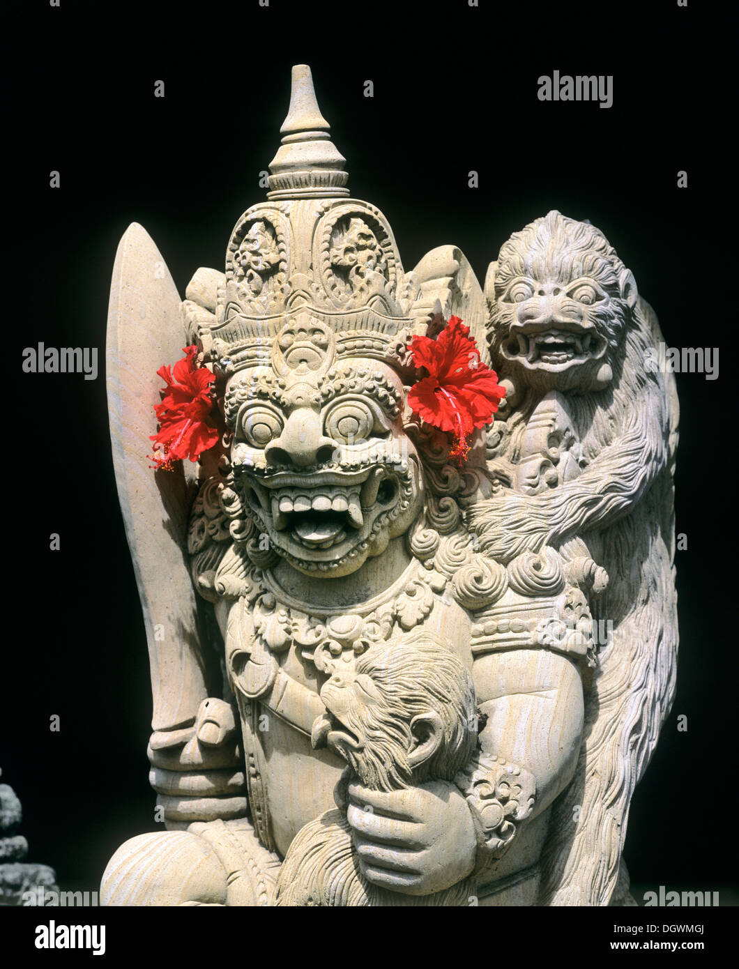 Demon's head carved out of stone decorated with red hibiscus flowers ...