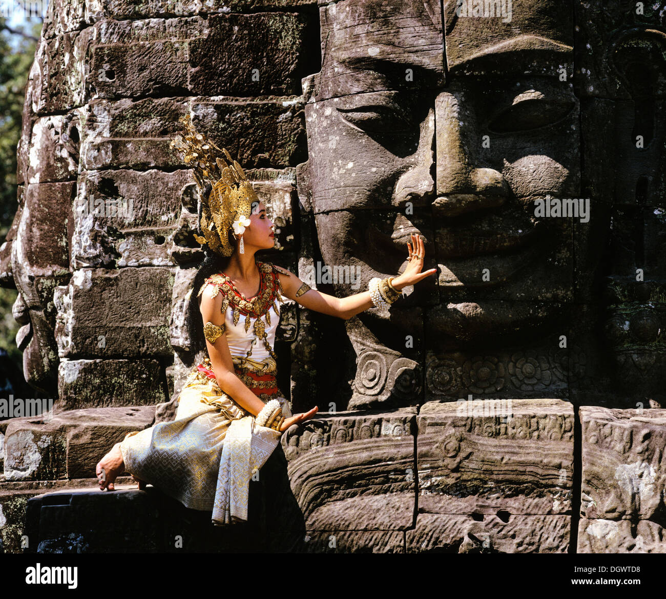 Temple dancer or apsara sitting in front of a face tower at Bayon ...