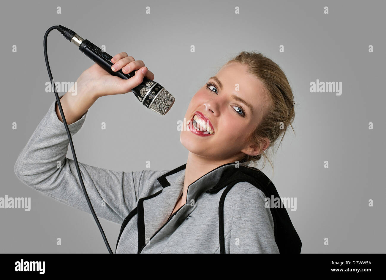 Young woman holding a microphone in a singer pose Stock Photo - Alamy