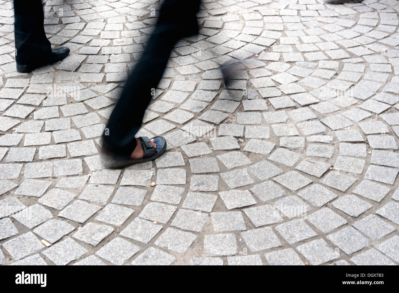 Movement of commuters feet (blurred), walking across cobbled pavement ...