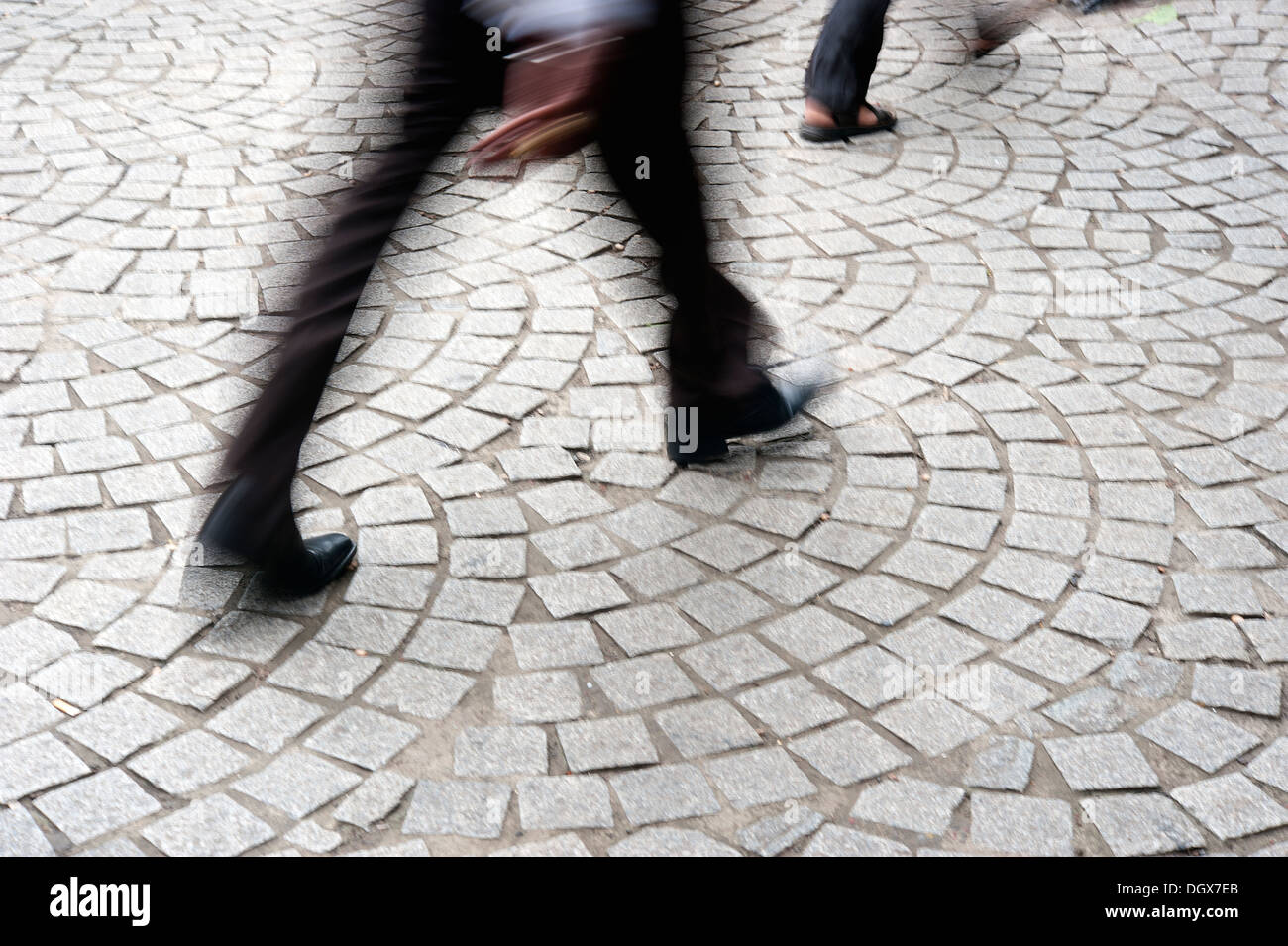 Movement of commuters feet (blurred), walking across cobbled pavement ...