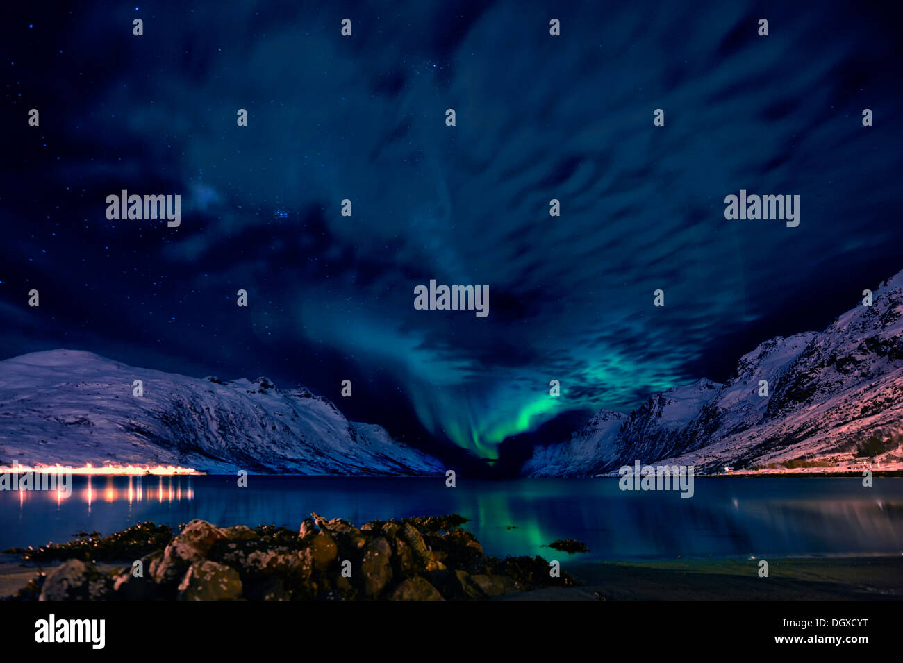 Aurora over a fjord with snow-covered mountains and an illuminated ...