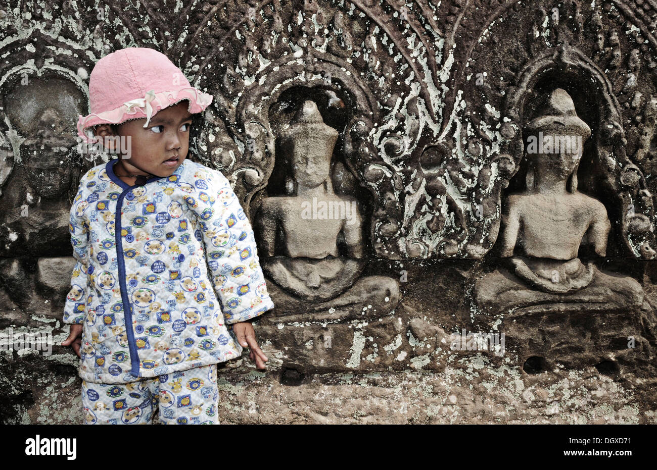 Child standing in front of Buddha stone carvings, Angkor Wat, Siem Reap ...