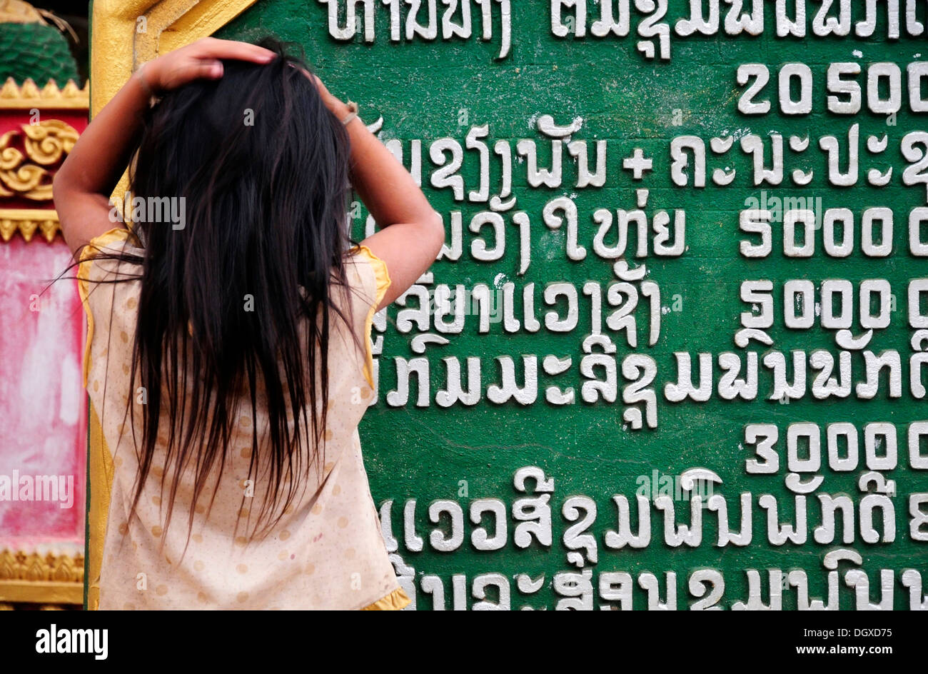 Child reading Asian lettering, hands on her head, Laos, Southeast Asia ...