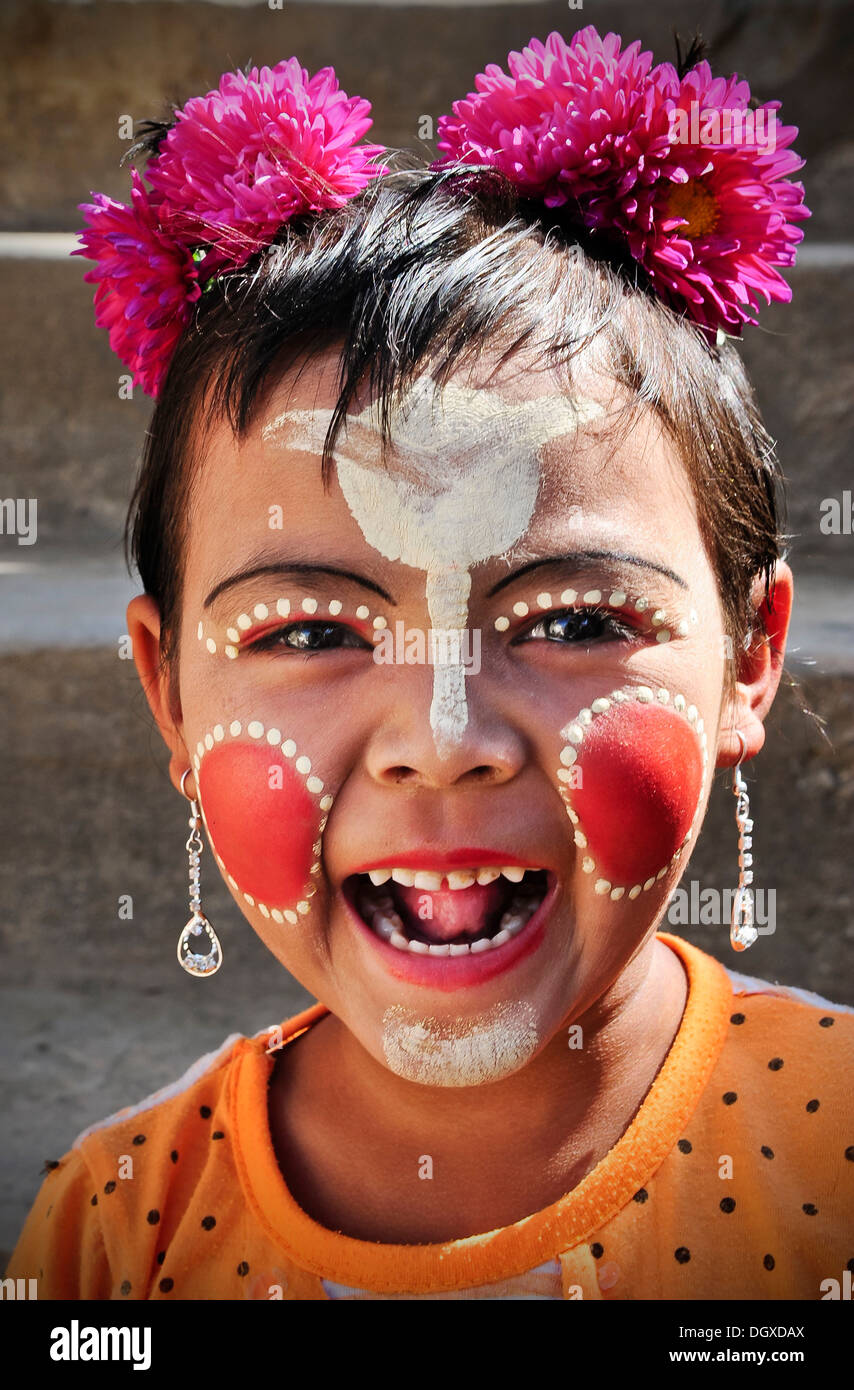 Girl, laughing, with flowers in her hair, her face is painted with ...