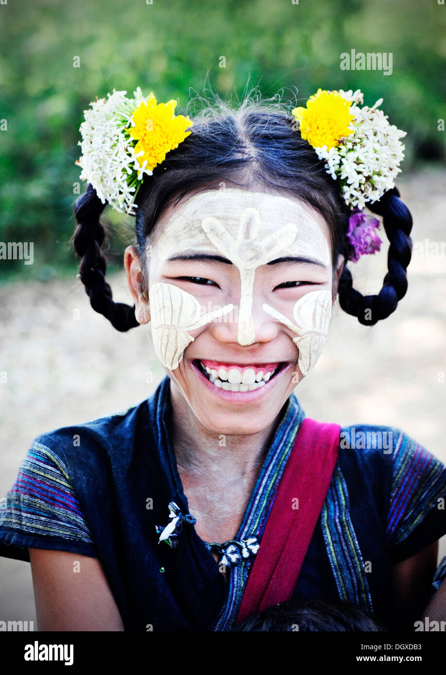 Smiling girl wearing thanaka paste on her face and flowers in her hair ...